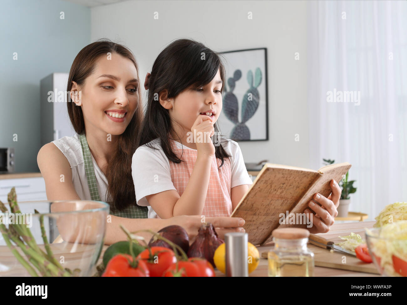 Mother with cute daughter reading cook book in kitchen Stock Photo - Alamy