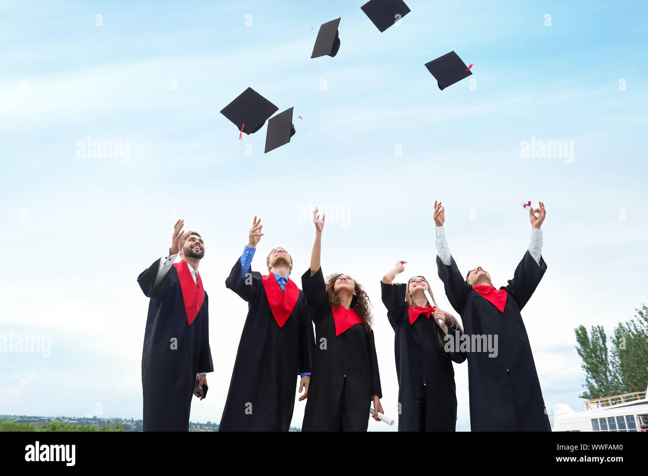 Happy students in bachelor robes throwing graduation hats outdoors ...