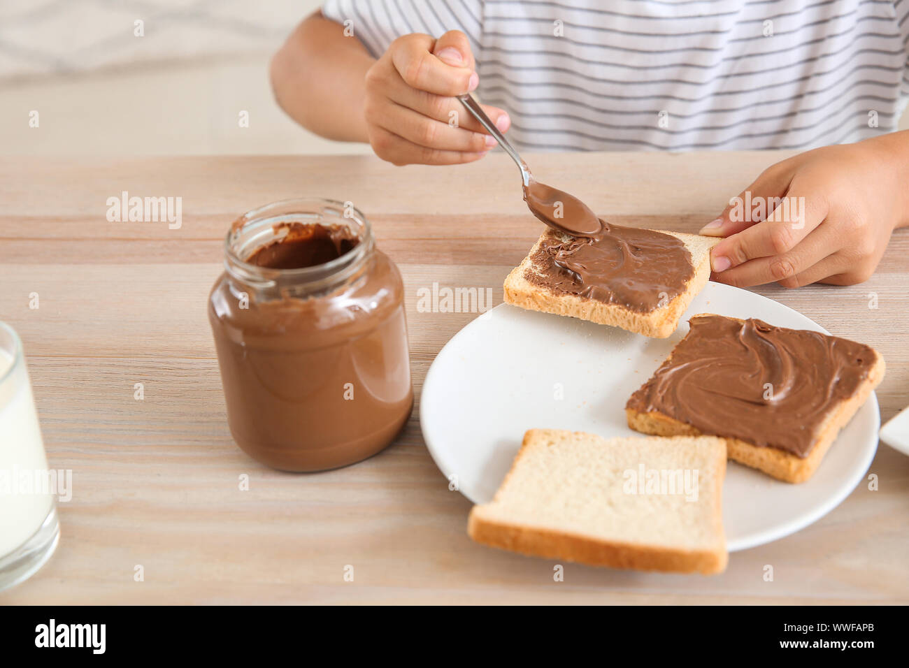 Funny little boy eating tasty toasts with chocolate spreading in ...