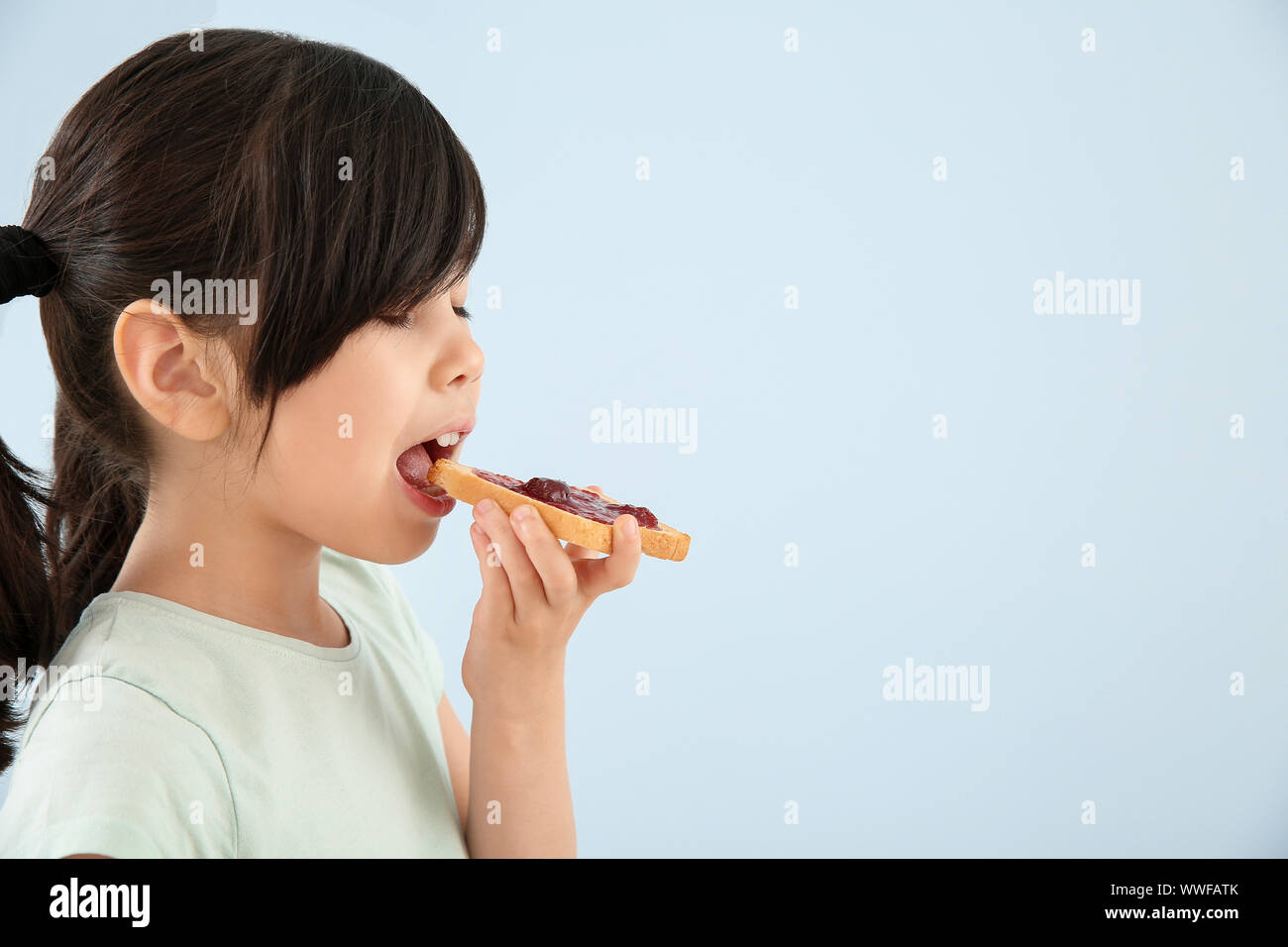 Funny little girl eating tasty toast on color background Stock Photo ...