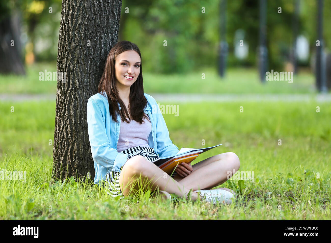 Beautiful female student sitting under tree in park Stock Photo - Alamy