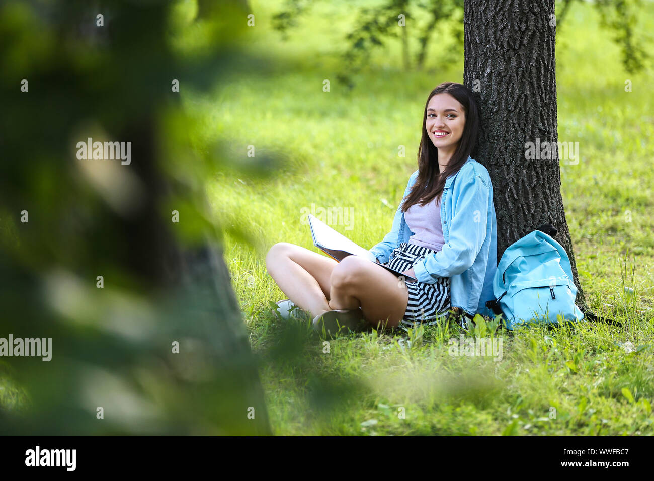 Beautiful female student sitting under tree in park Stock Photo - Alamy