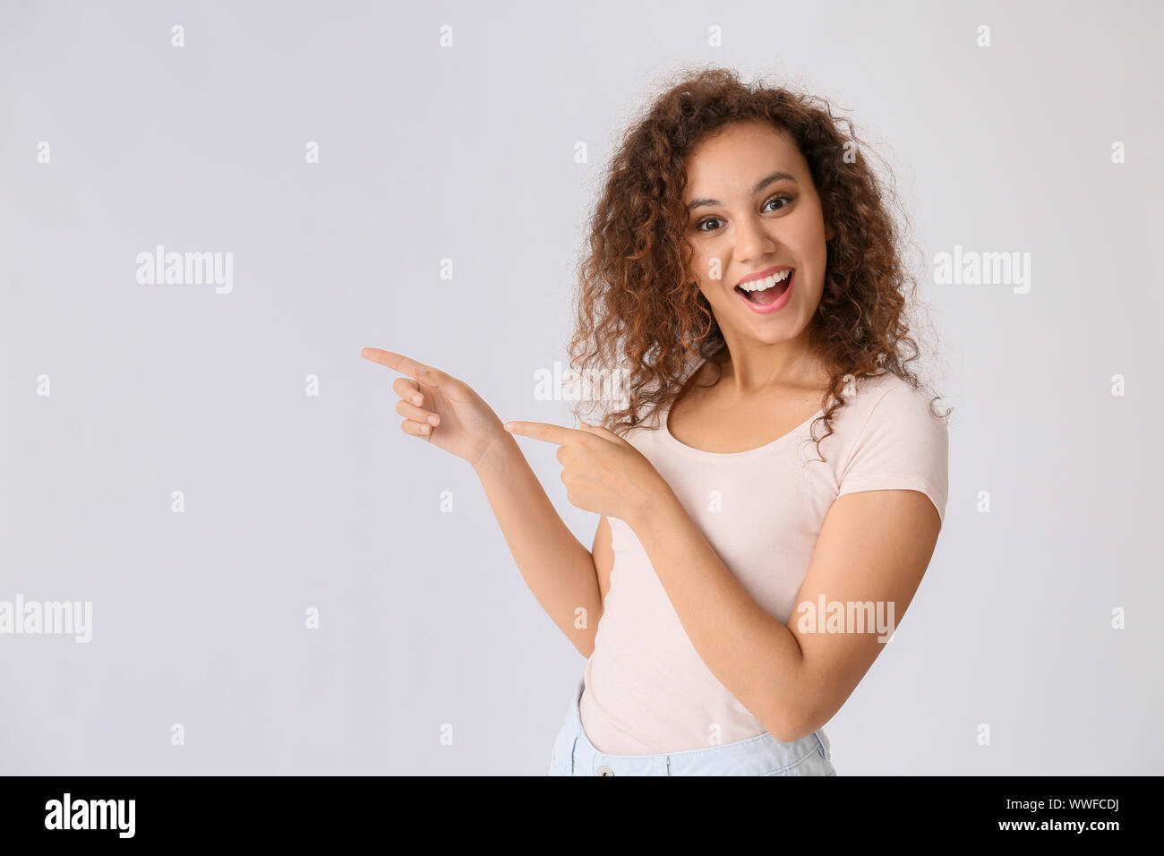 Beautiful African-American woman pointing at something on white ...