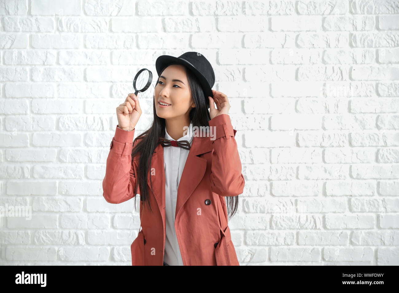Female Asian detective with magnifying glass against white brick wall ...