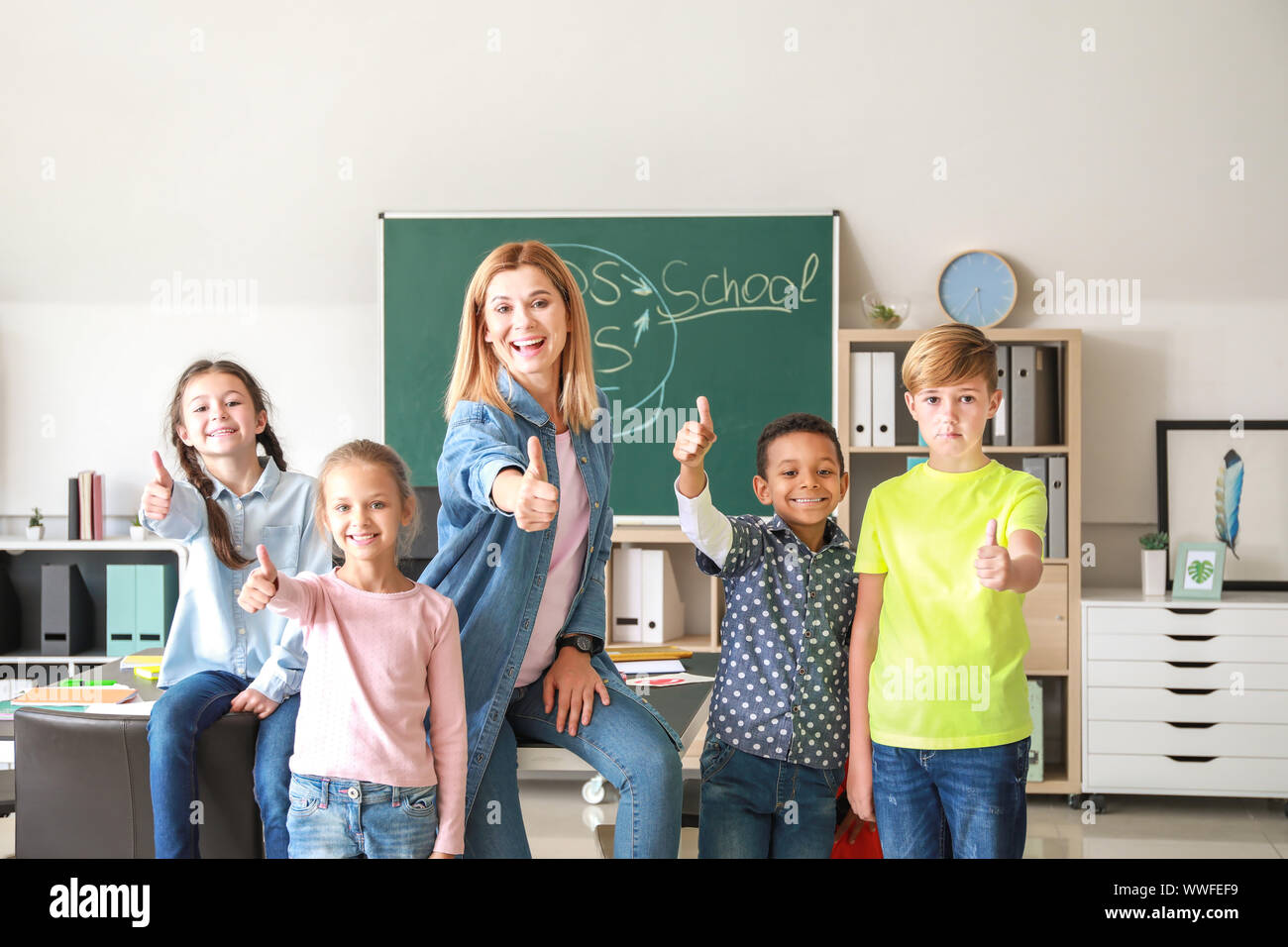 Cute children with teacher showing thumb-up gesture in classroom Stock ...