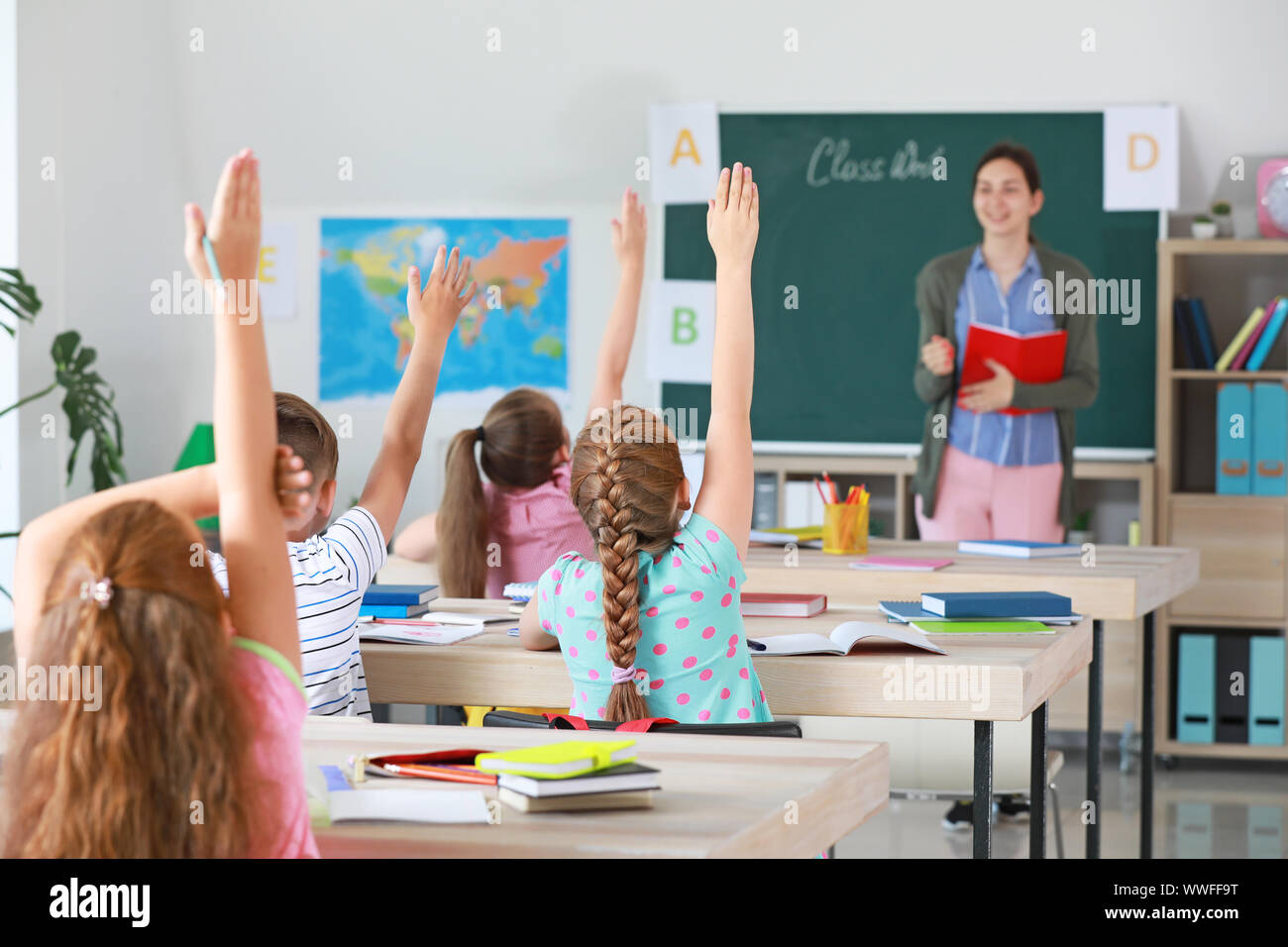 Cute little pupils raising hands during lesson in classroom Stock Photo ...