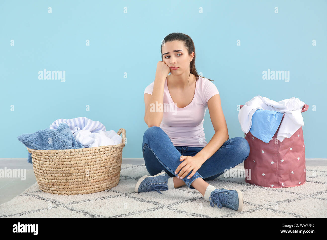 Upset young woman with laundry sitting on floor near color wall Stock ...