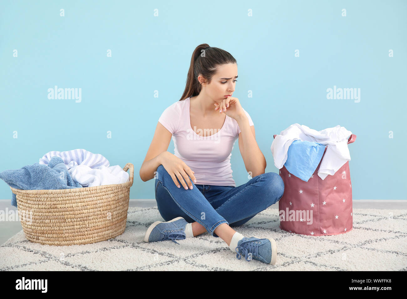 Upset young woman with laundry sitting on floor near color wall Stock ...
