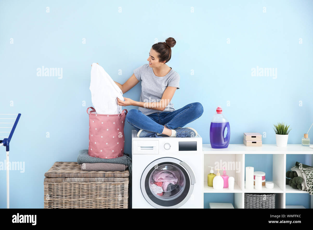 Beautiful young woman with clean laundry sitting on washing machine at ...