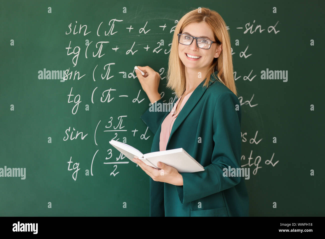 Beautiful math teacher with book near blackboard in classroom Stock ...