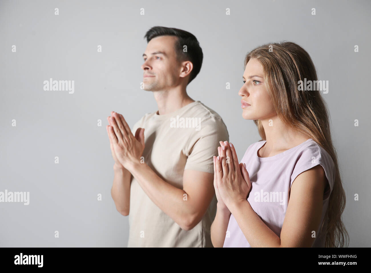 Religious couple praying to God on grey background Stock Photo - Alamy