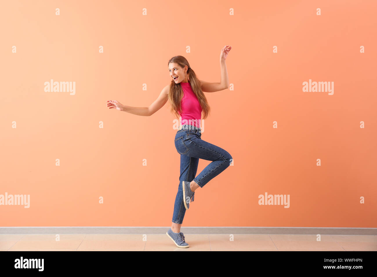 Beautiful young woman dancing against color wall Stock Photo - Alamy