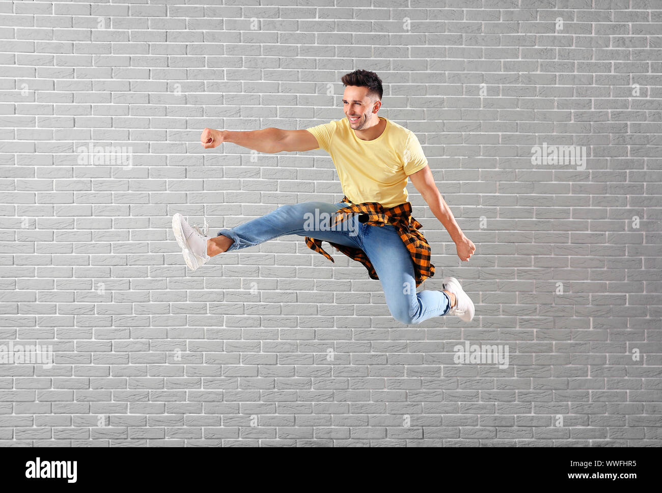 Handsome young man jumping against brick wall Stock Photo - Alamy