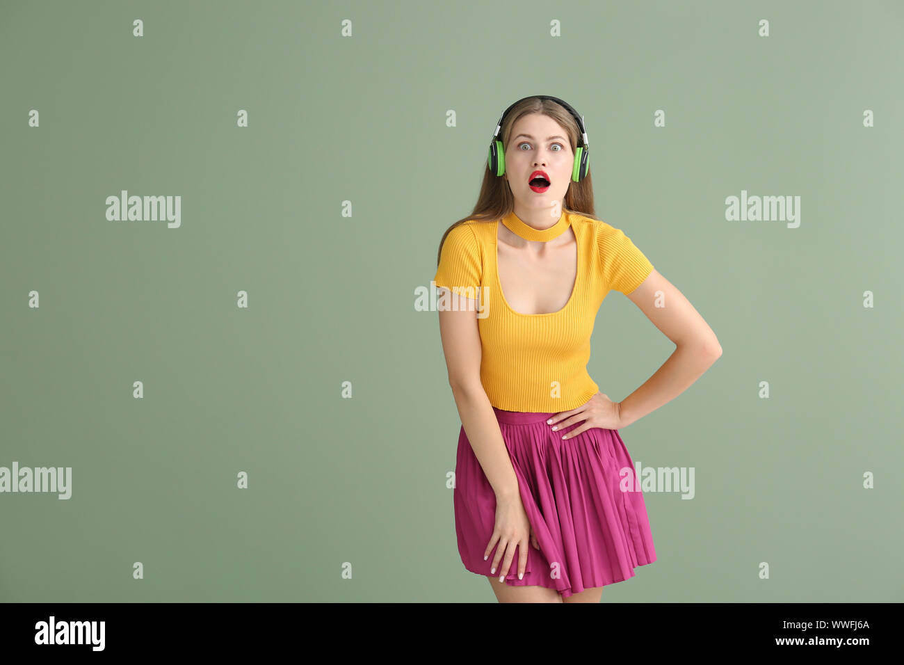 Shocked young woman listening to music on color background Stock Photo ...