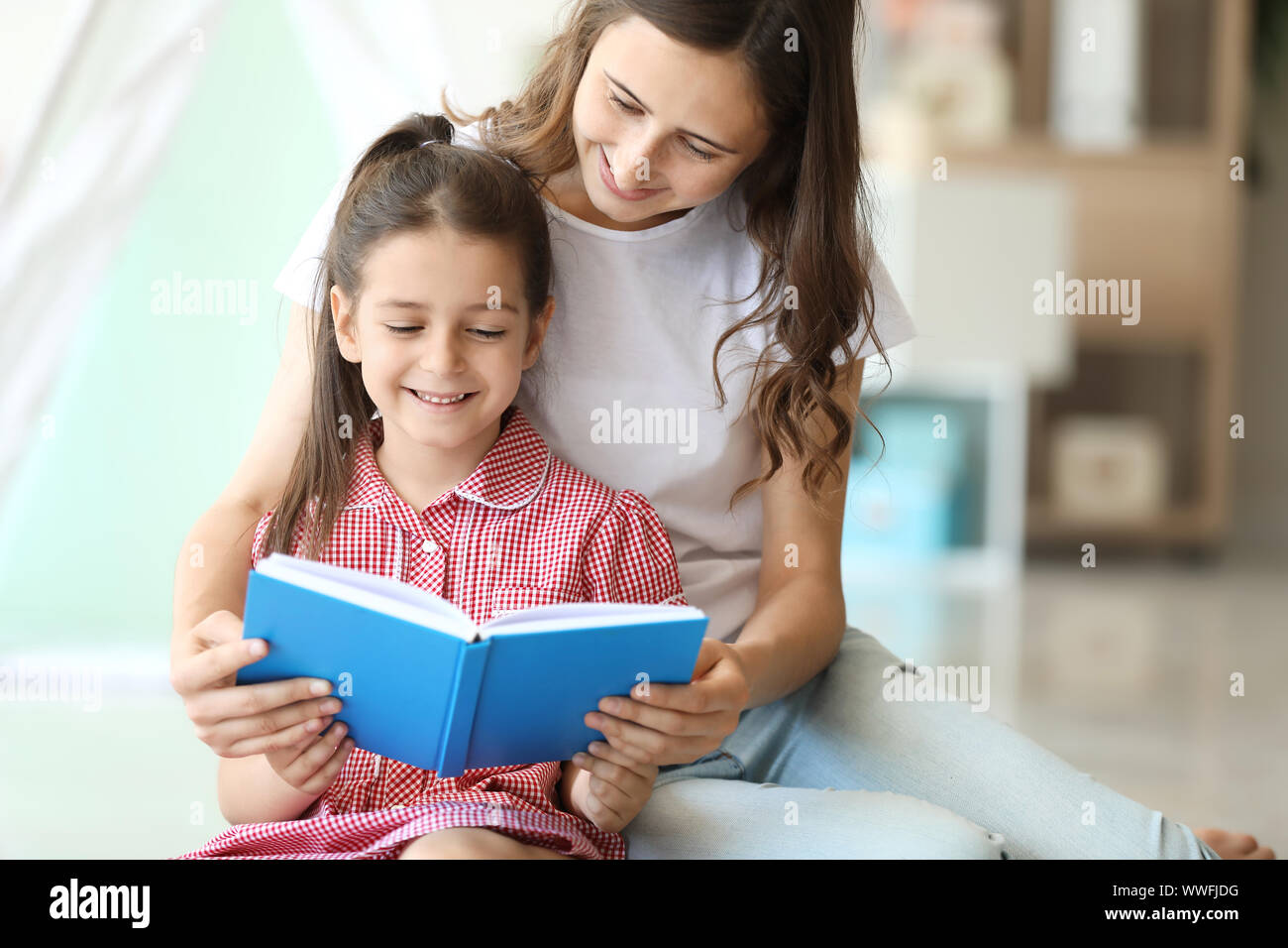 Cute little girl and her elder sister reading book at home Stock Photo ...