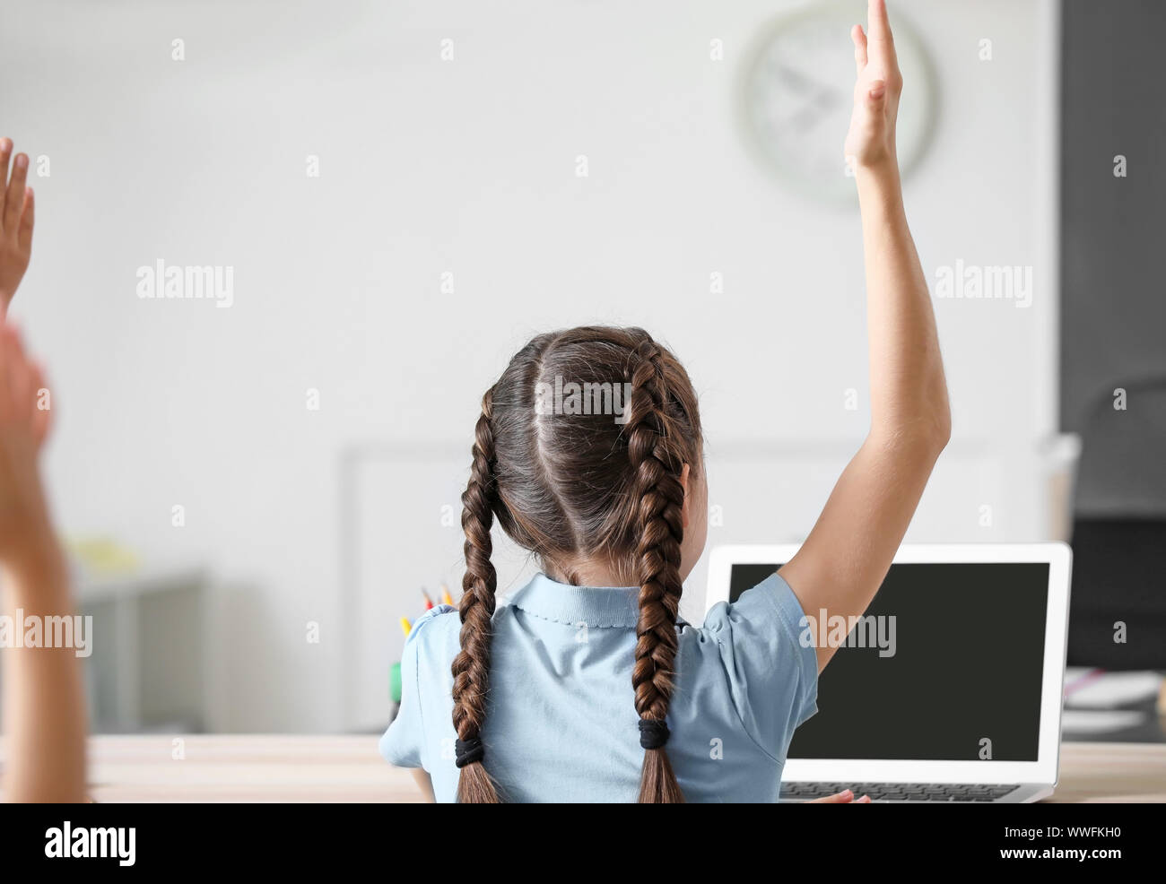 Cute little girl raising hand in classroom Stock Photo - Alamy