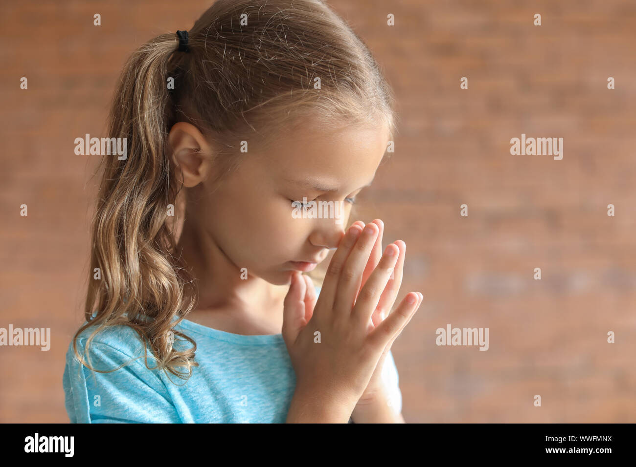 Cute little girl praying against blurred background Stock Photo - Alamy