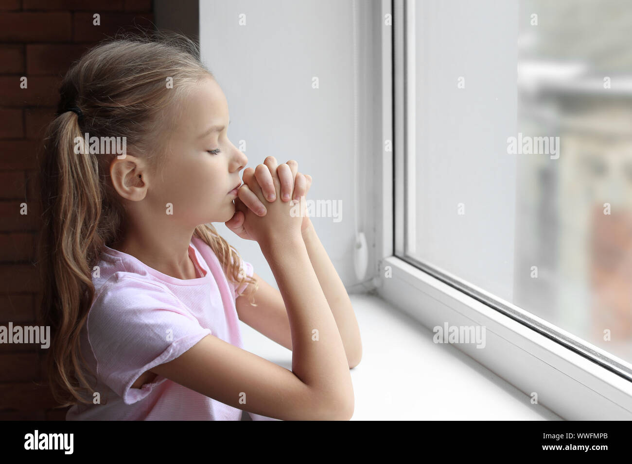 Praying little girl near window Stock Photo - Alamy