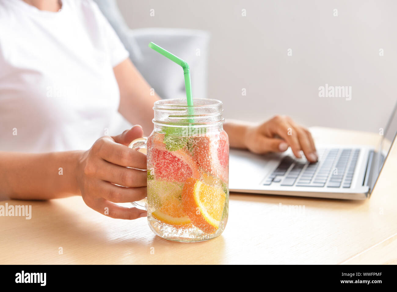 Woman drinking infused water while working on laptop at table Stock ...