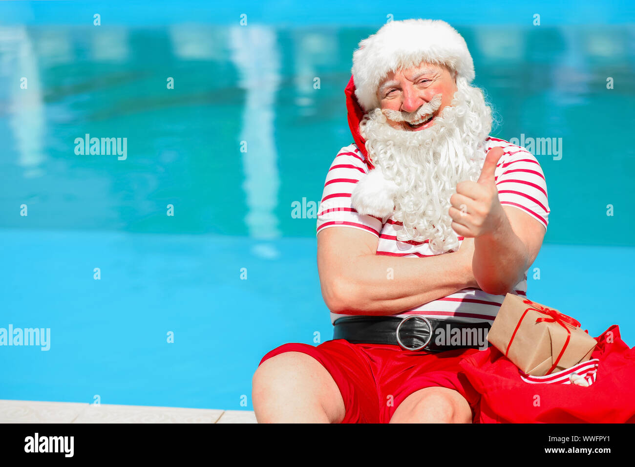 Santa Claus with gifts showing thumb-up near swimming pool at resort ...