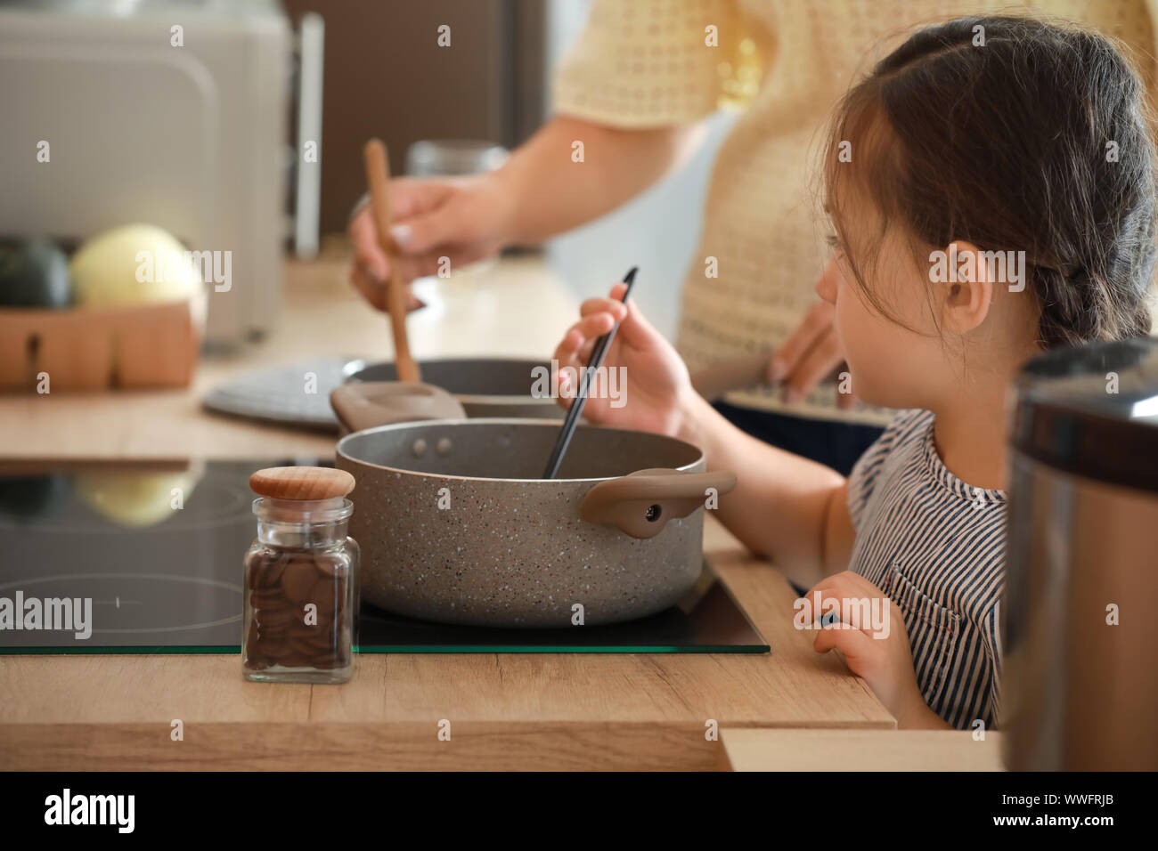 Little daughter with mother cooking soup in kitchen Stock Photo - Alamy