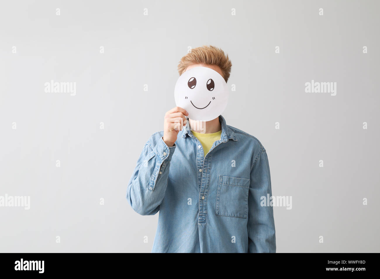 Man hiding face behind emoticon on light background Stock Photo - Alamy