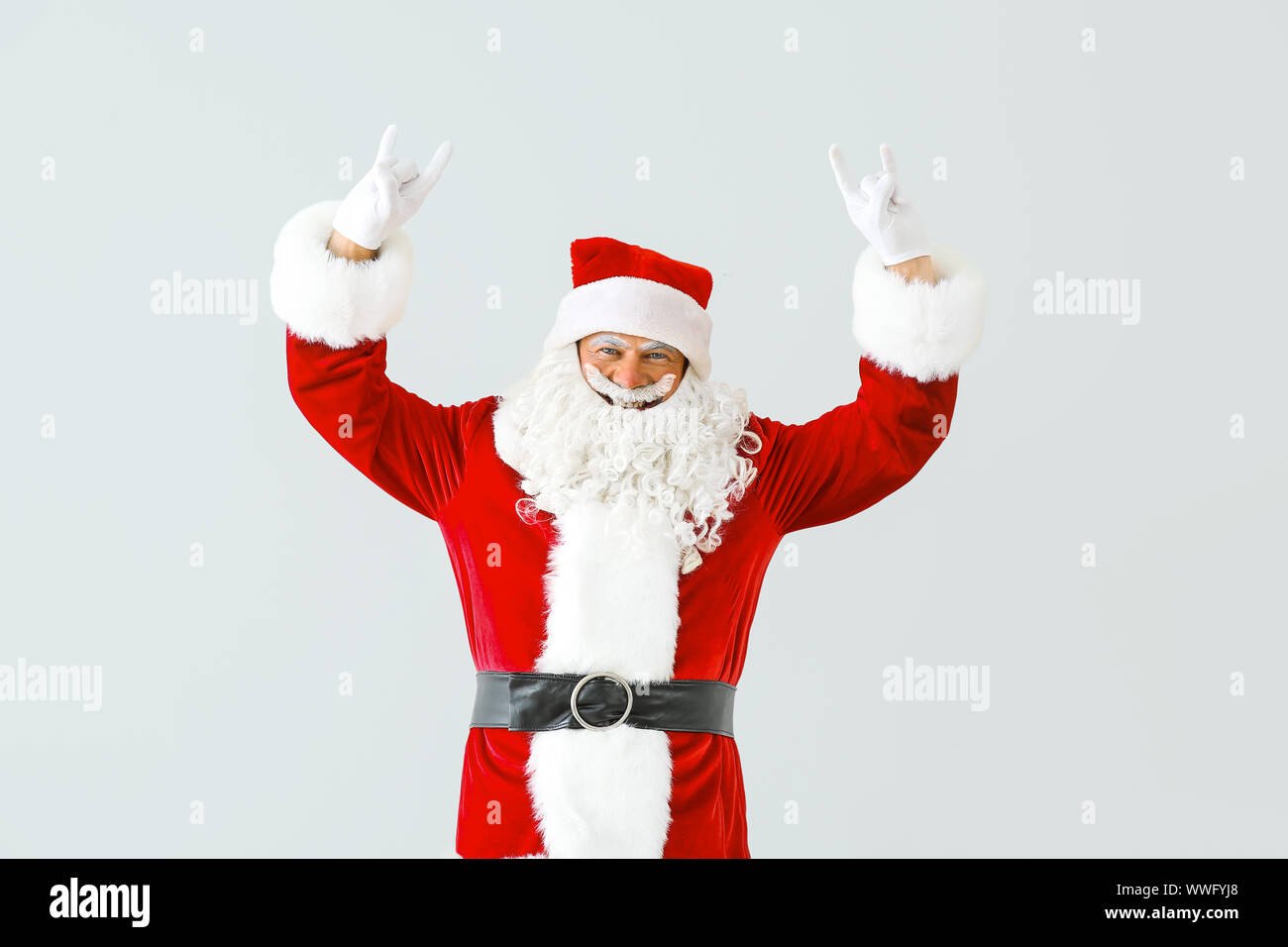 Portrait of cool Santa Claus showing "devil horns" gesture on light ...
