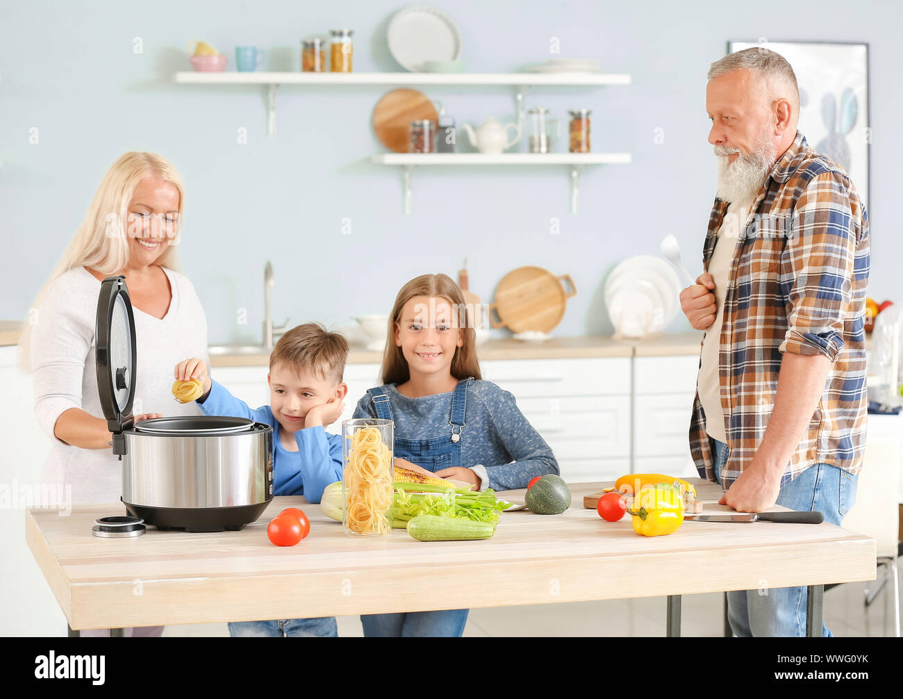 Grandparents and little children using modern multi cooker in kitchen ...