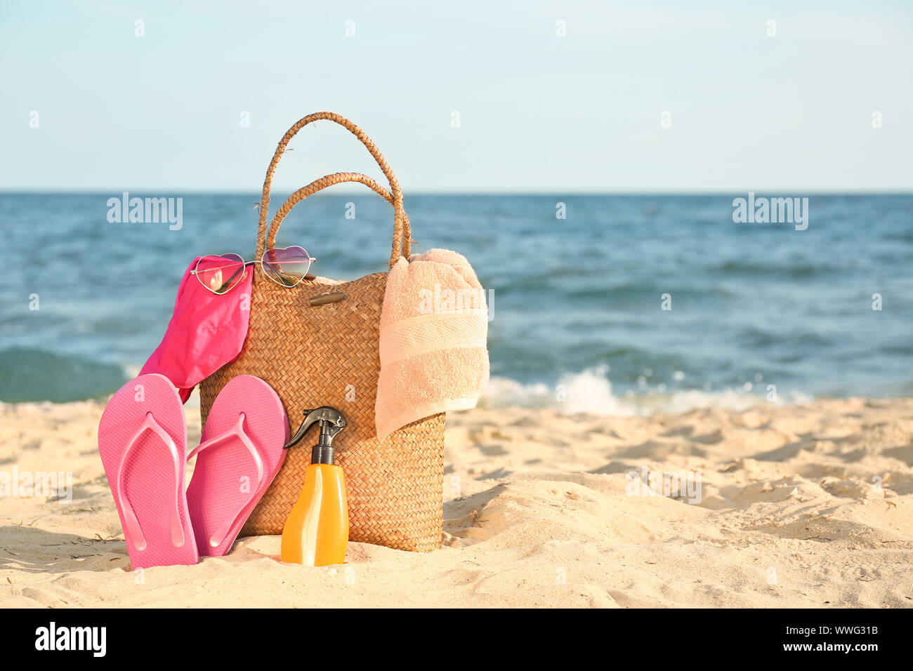 Bag with flip-flops, swimsuit, towel, sunglasses and cosmetics on sand ...