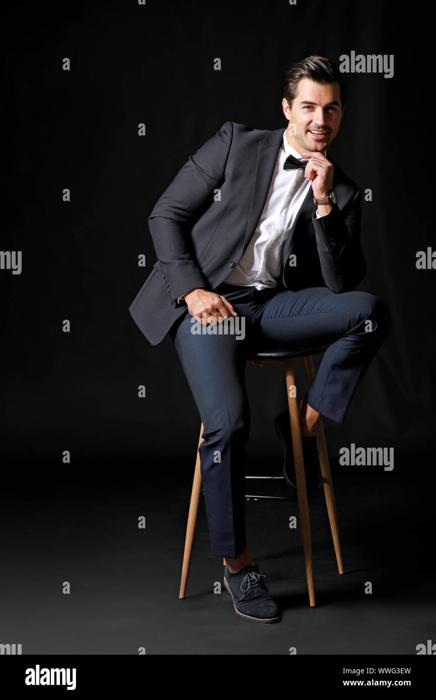 Fashionable man in formal clothes sitting on chair against dark ...