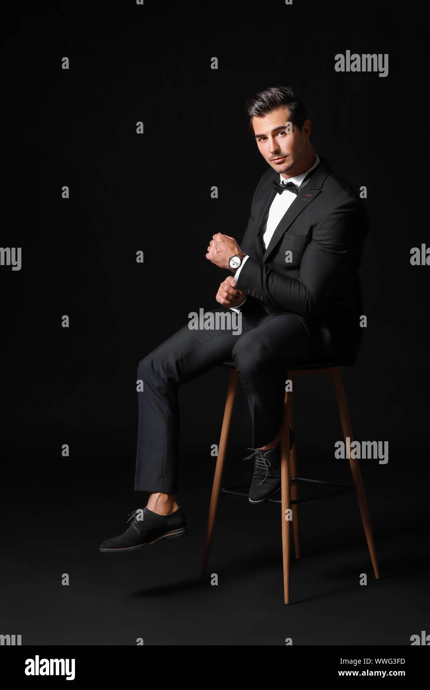 Fashionable man in formal clothes sitting on chair against dark ...