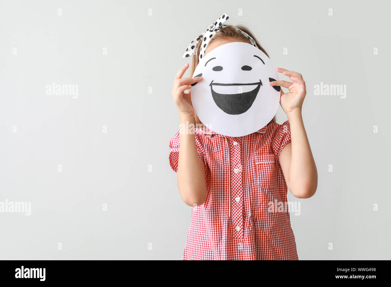 Little girl hiding face behind drawn emoticon on light background Stock ...
