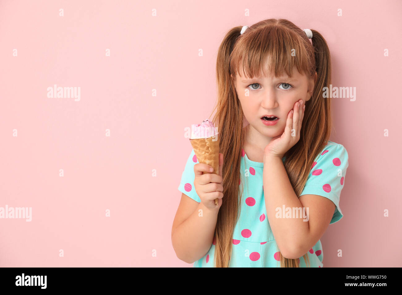 Little girl with sensitive teeth and cold ice-cream on color background ...
