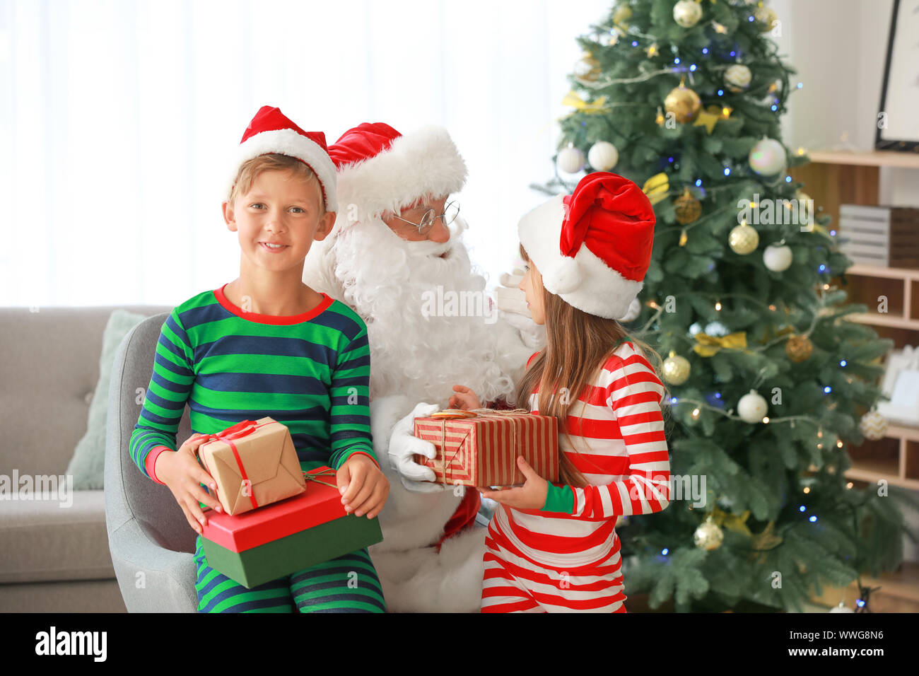 Santa Claus and his little helpers with gifts in room decorated for ...