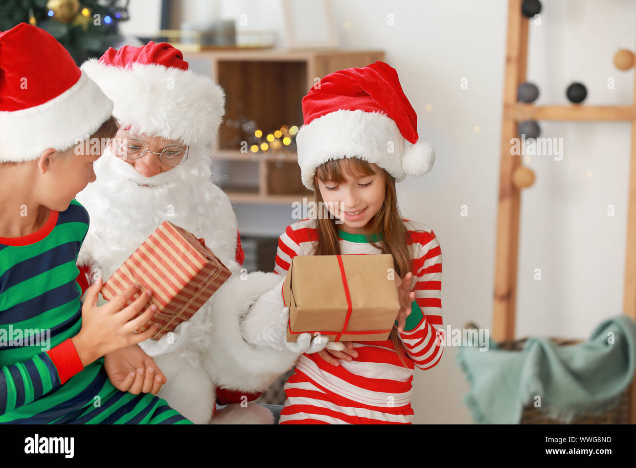 Santa Claus and his little helpers with gifts in room decorated for ...