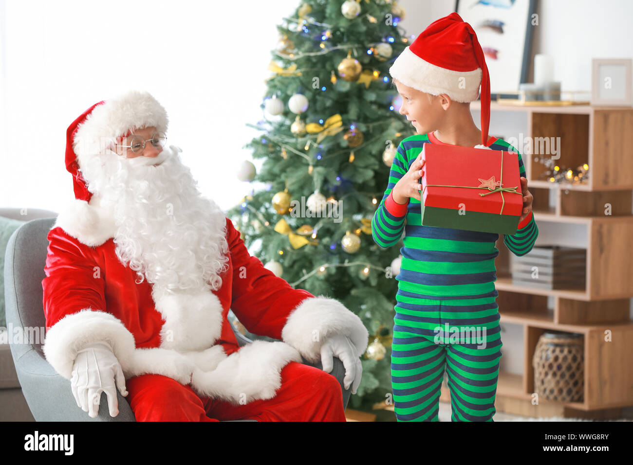 Santa Claus and little elf kid with gift in room decorated for ...