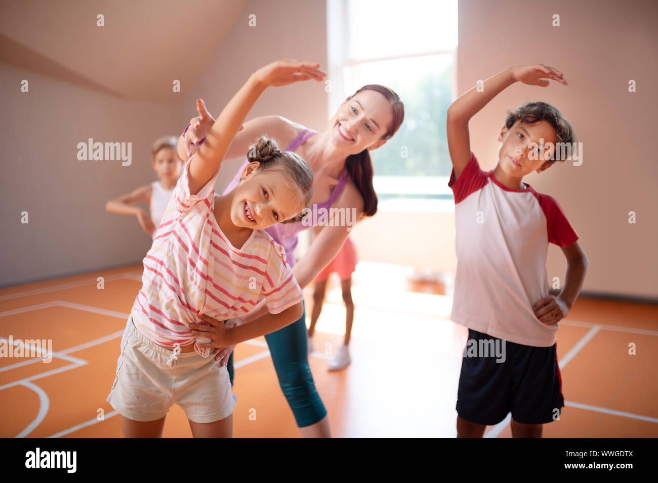 Smiling teacher helping girl stretching body at PE lesson Stock Photo ...