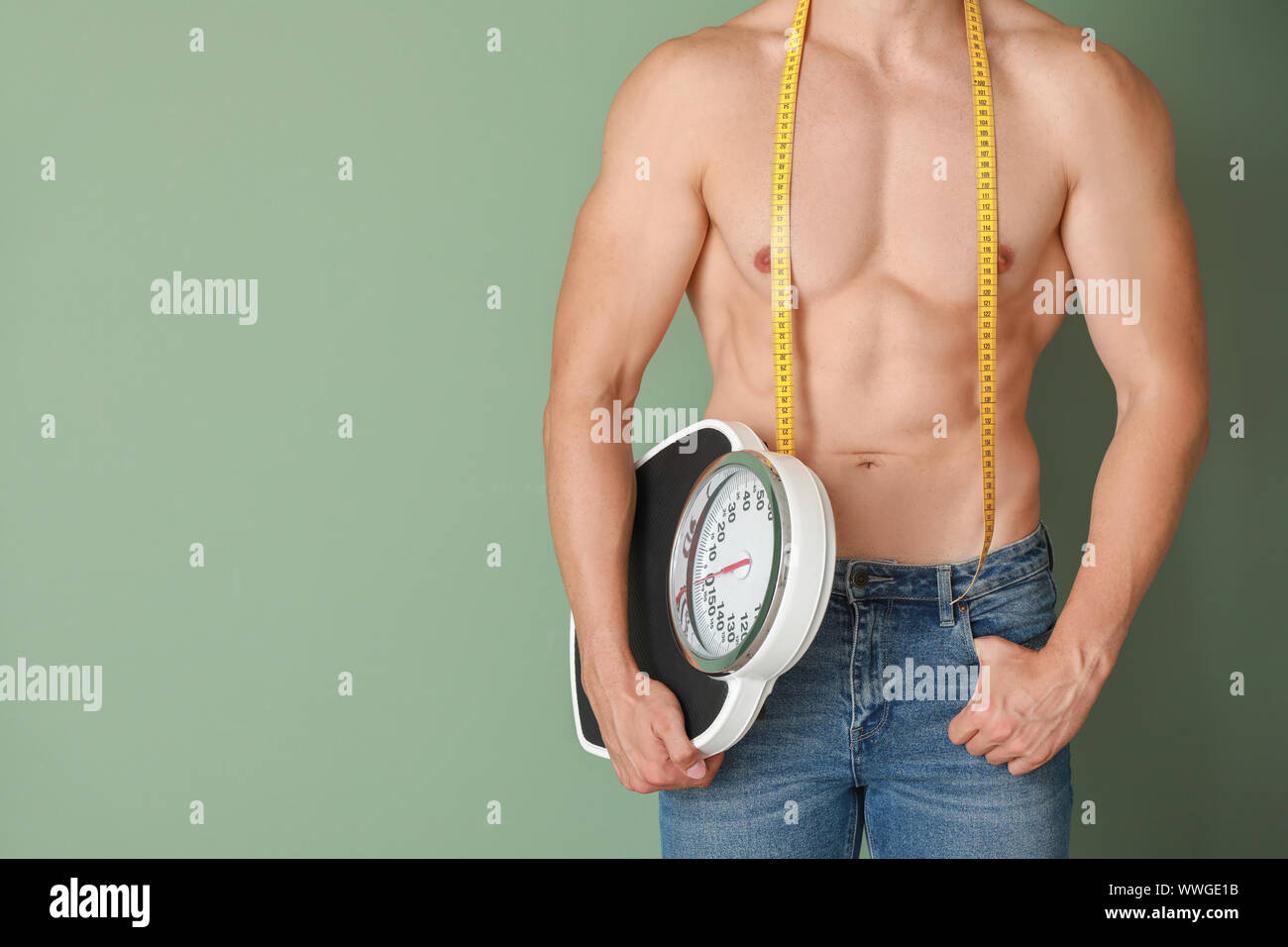 Handsome muscular man with measuring tape and scales on color ...