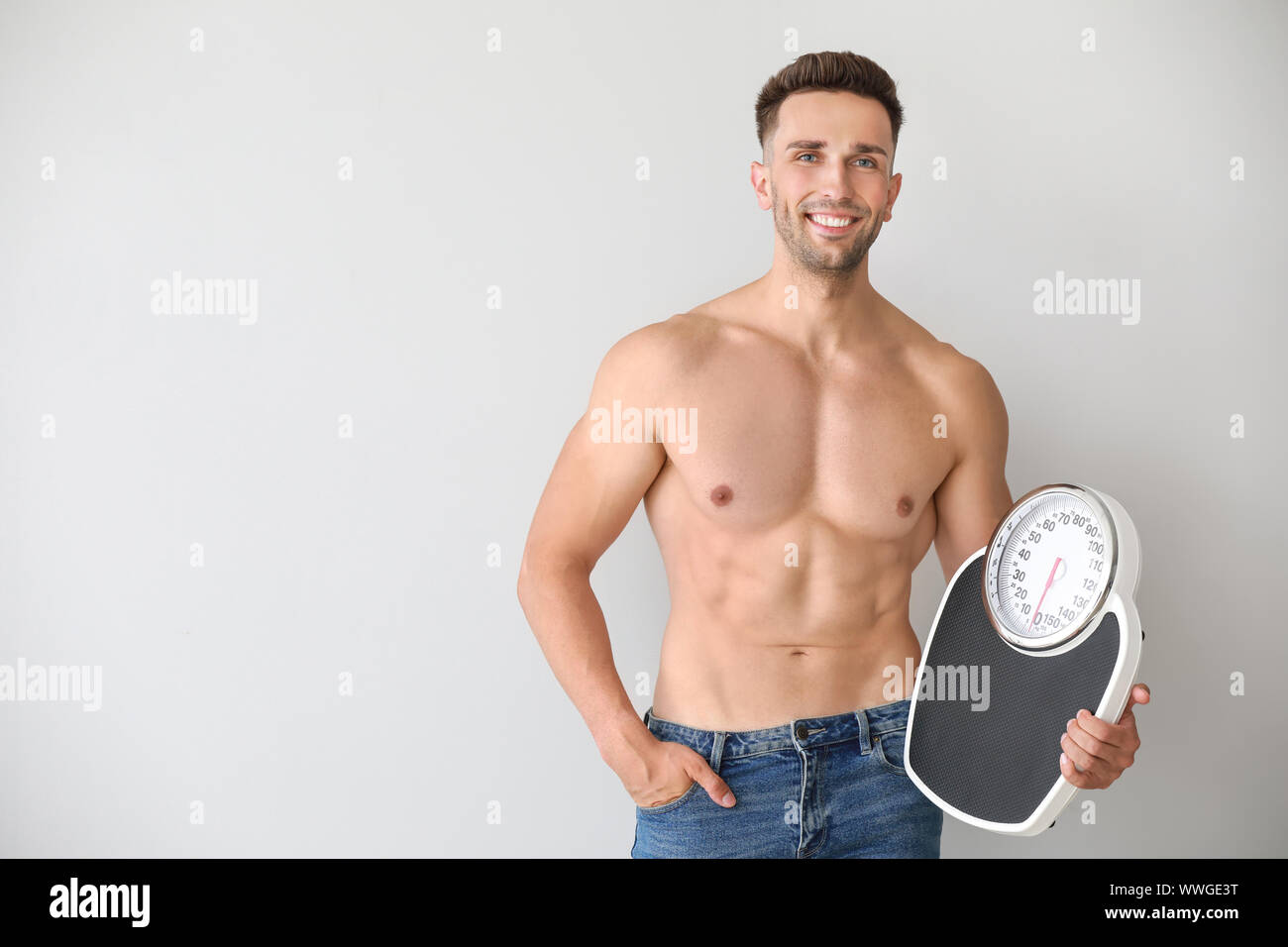 Handsome muscular man with scales on light background. Weight loss ...