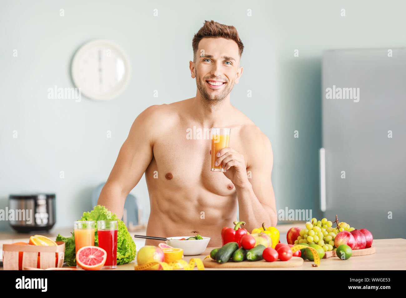 Handsome muscular man drinking juice in kitchen. Weight loss concept ...