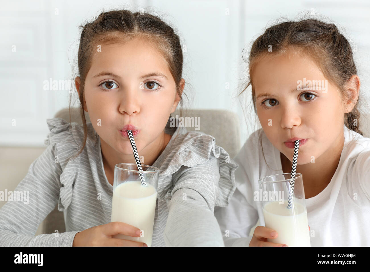 Portrait of cute twin girls drinking milk in kitchen Stock Photo - Alamy