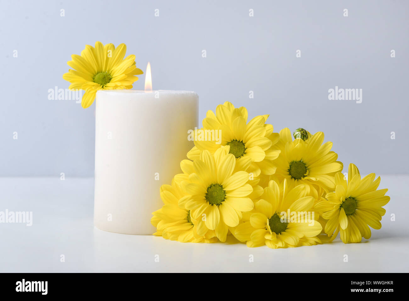Burning candle with fresh flowers on light background Stock Photo - Alamy