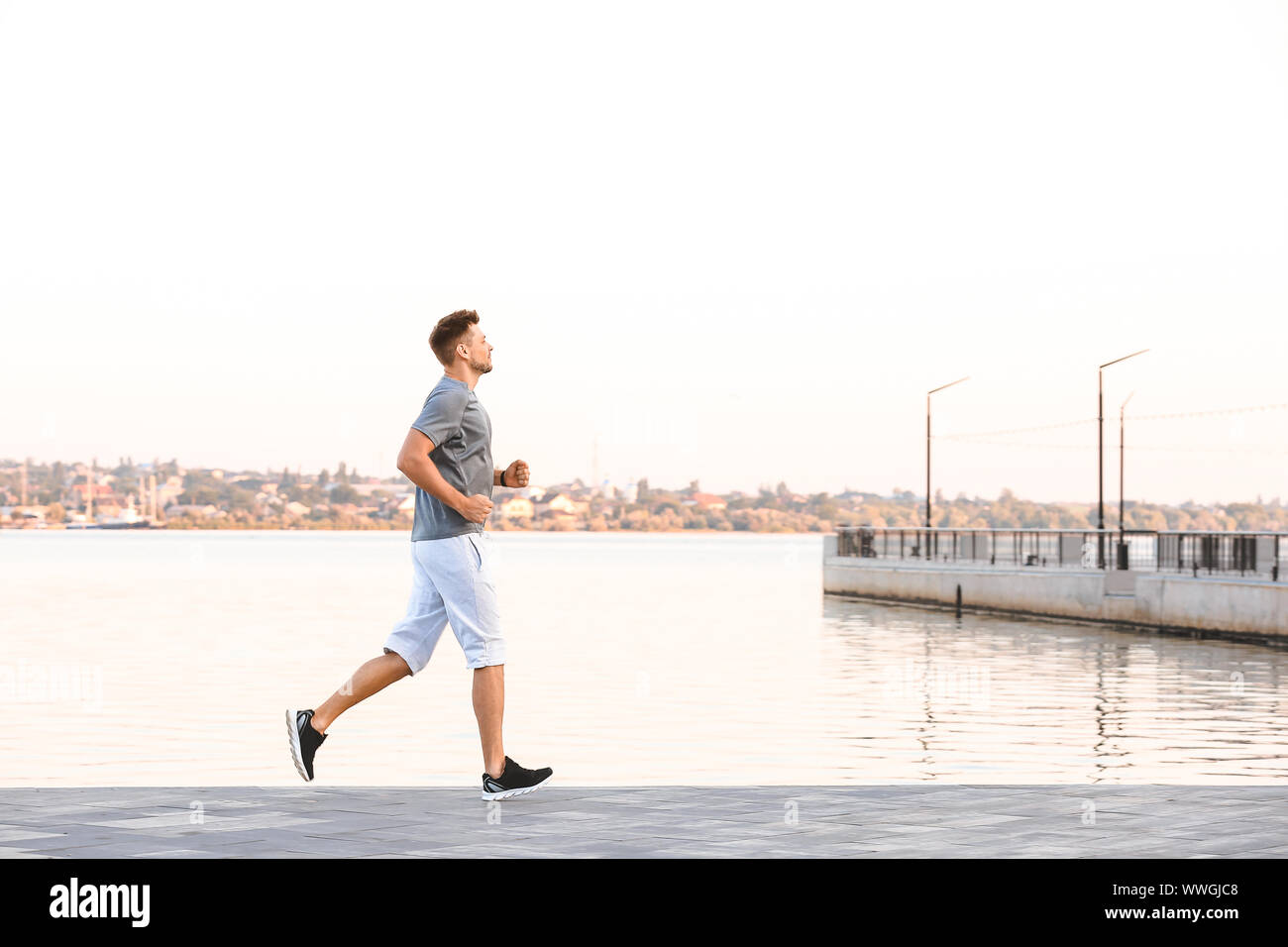 Handsome sporty man running near river Stock Photo - Alamy
