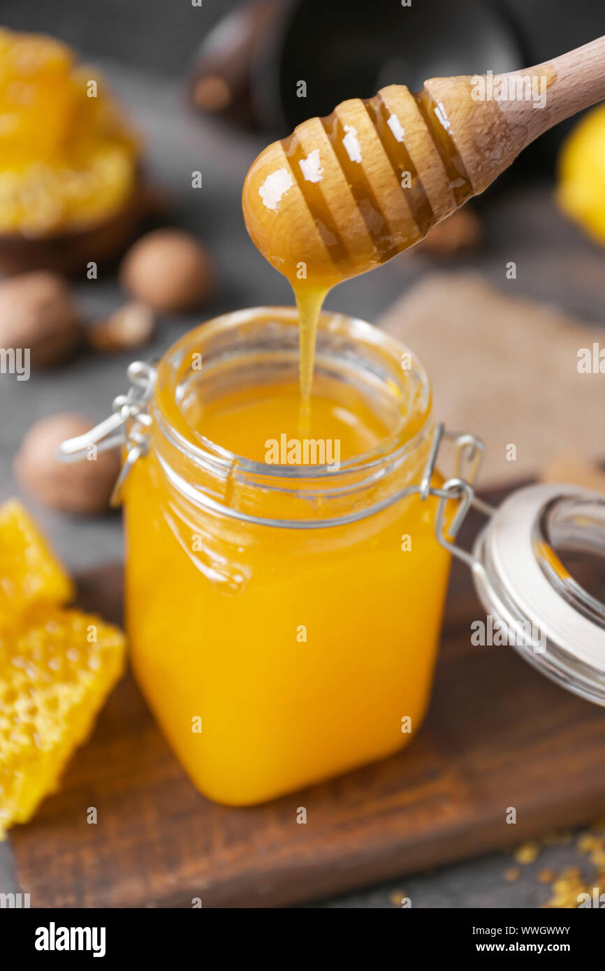 Honey pouring from dipper into jar on table Stock Photo - Alamy