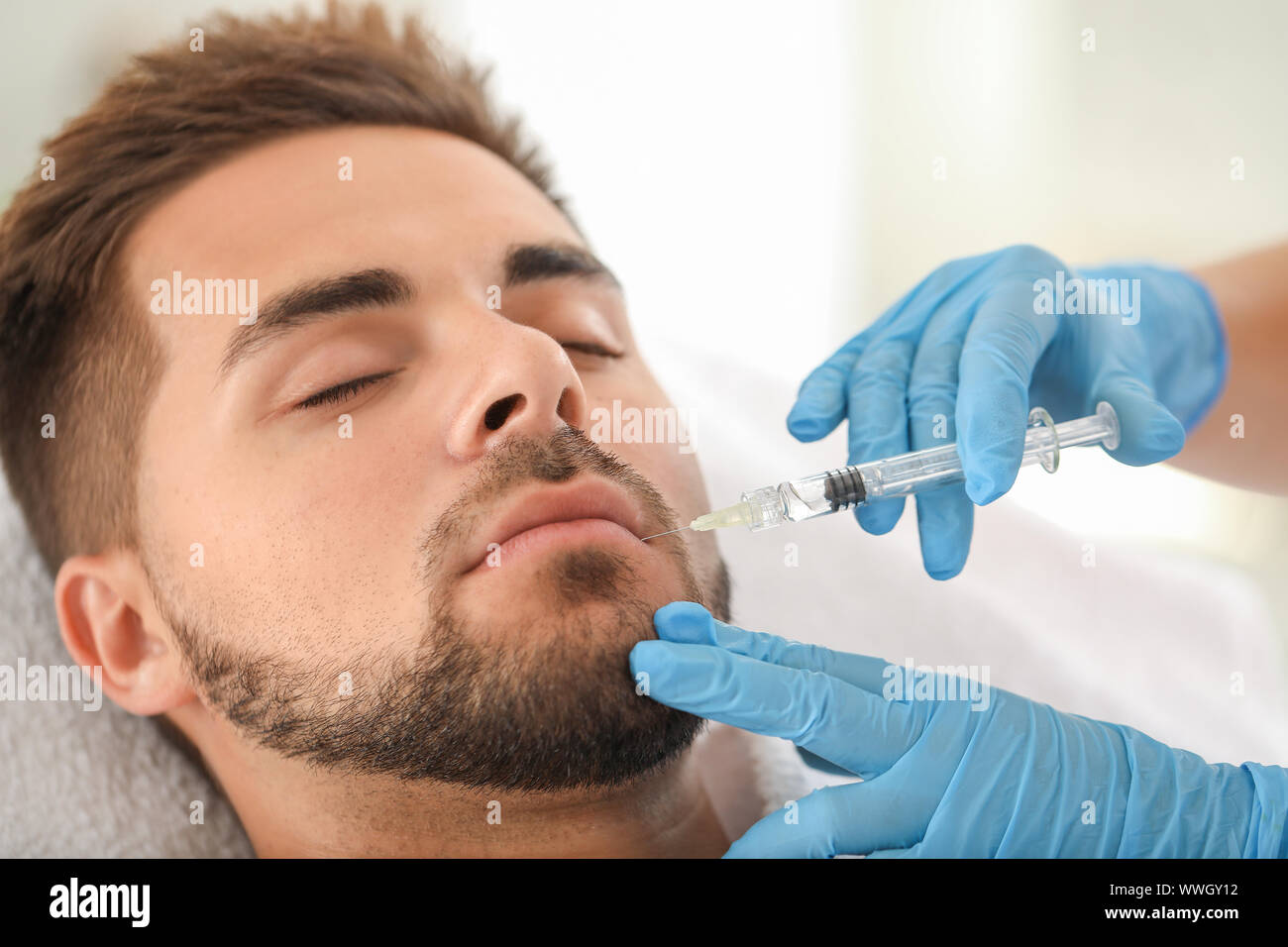 Handsome man receiving filler injection in beauty salon Stock Photo - Alamy