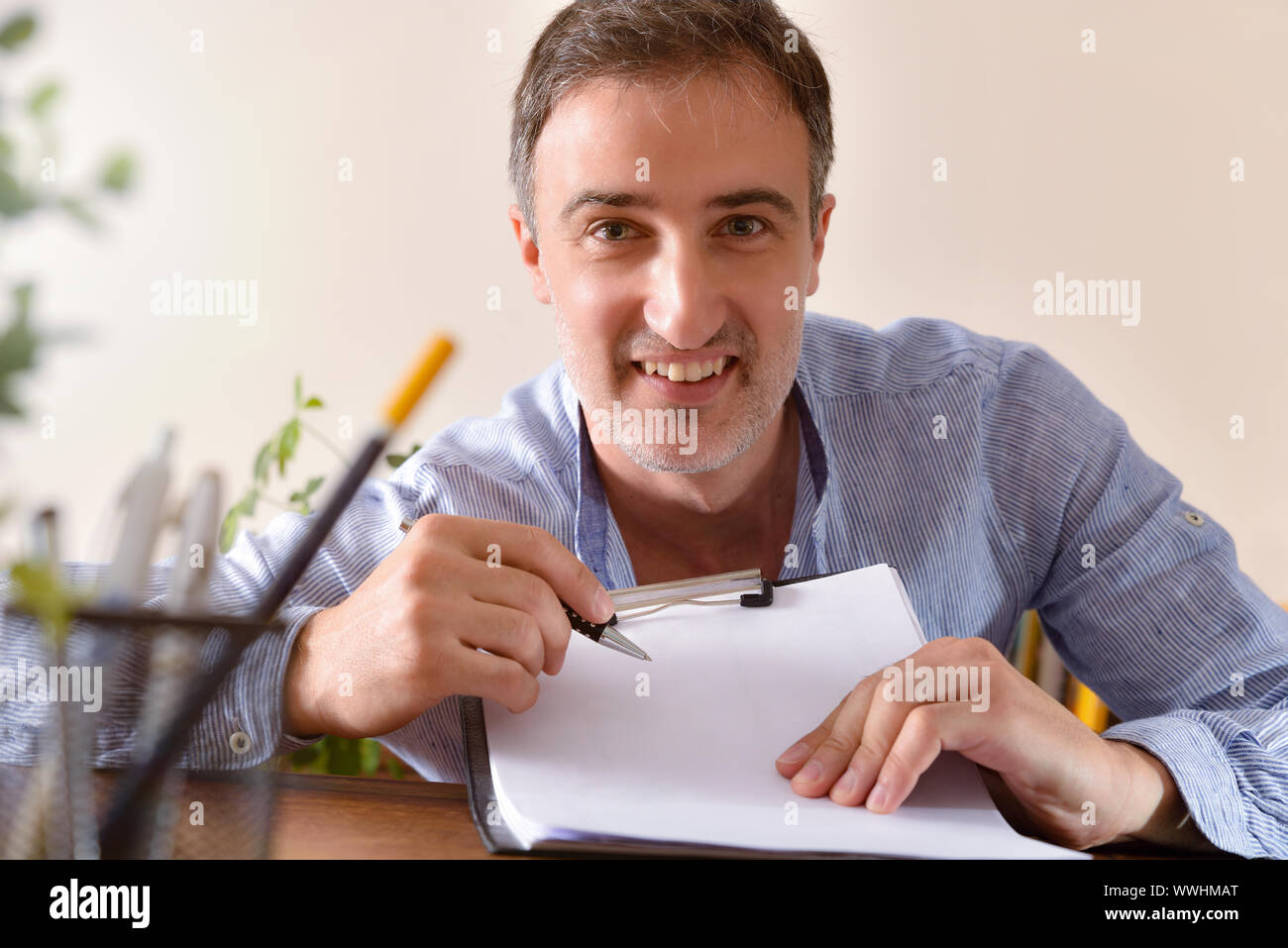 Smiling man showing blank sheet of paper in a folder sitting in front ...