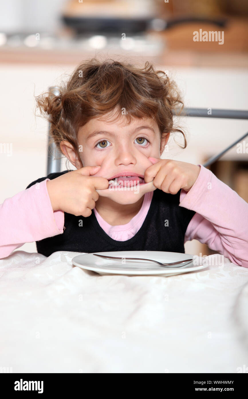 Little girl pulling a face at the table Stock Photo - Alamy