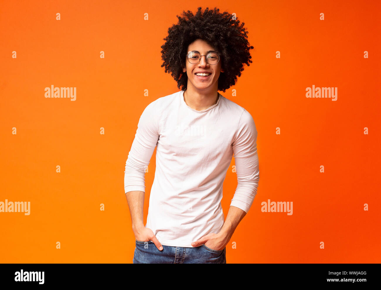 Carefree millennial curly guy posing with hands in jeans pockets Stock ...