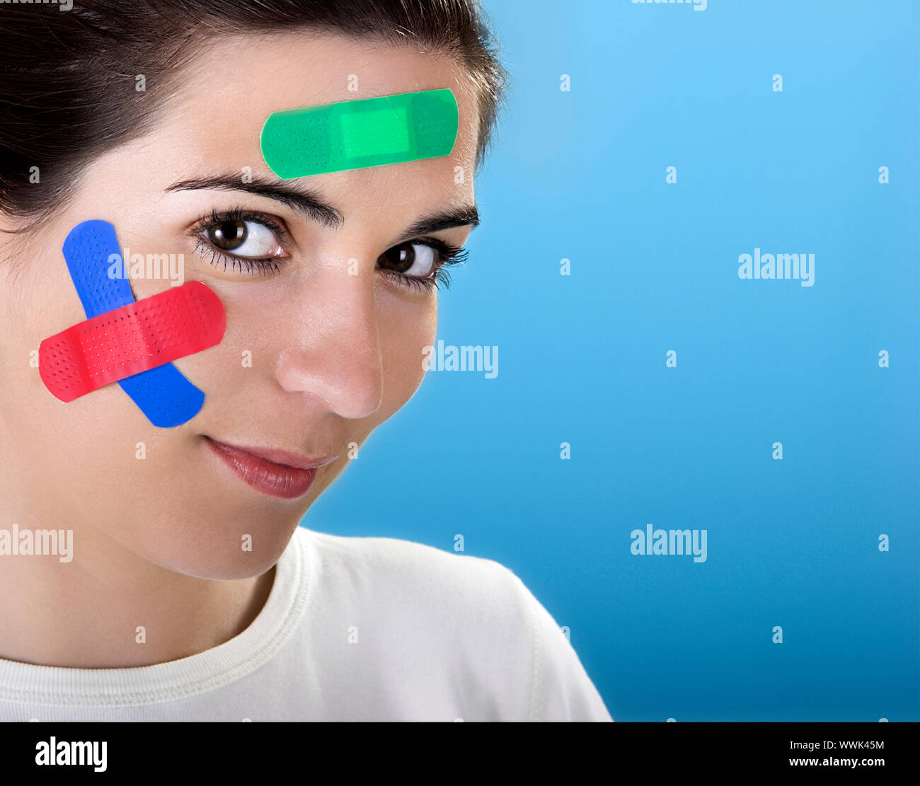 Beautiful woman with colored bandages on the face over a blue ...