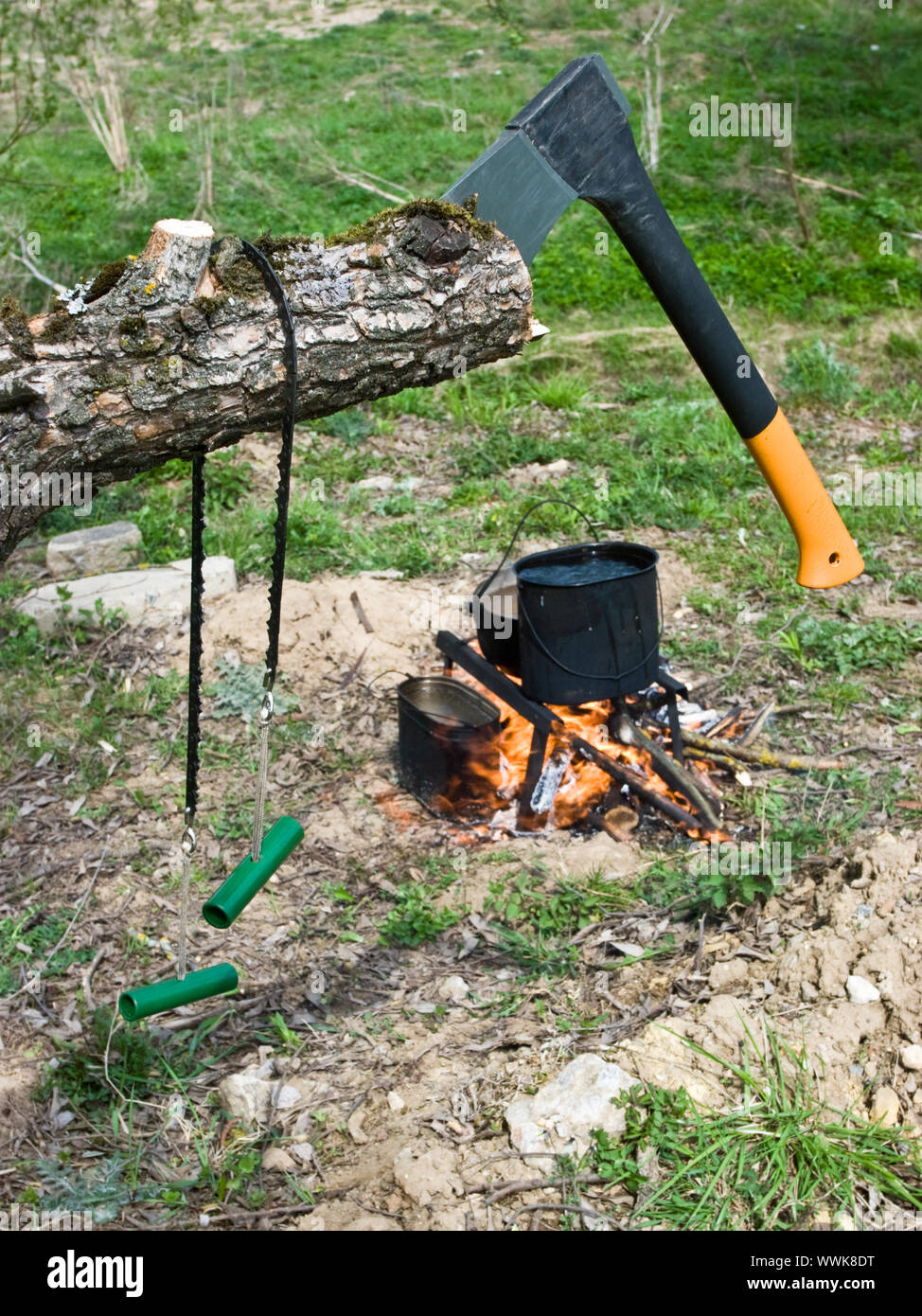 Hand saw and axe stuck in a tree, kettle with boiling water over ...